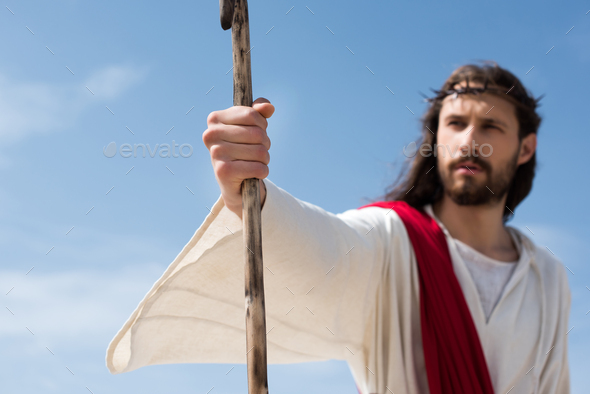 selective focus of Jesus in robe, red sash and crown of thorns holding ...