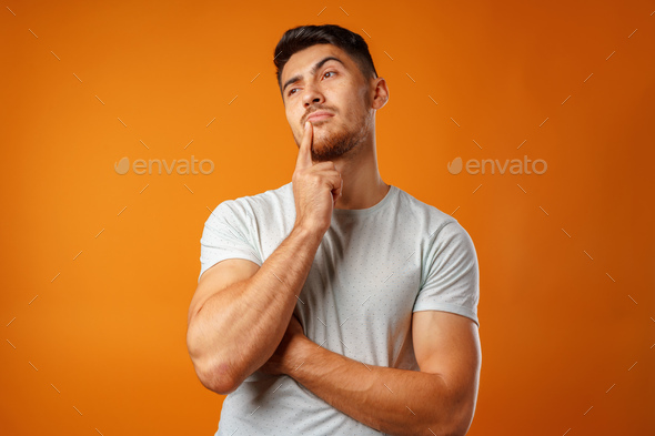 Photo of thoughtful young man touching his chin Stock Photo by FabrikaPhoto