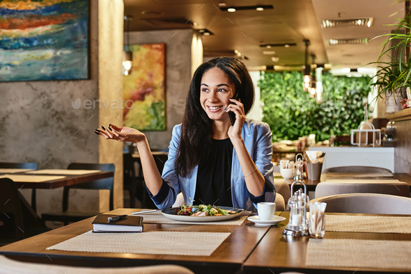 Businesswoman is talking on the phone, while having lunch in company's ...