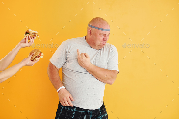 Funny overweight man in sportive head tie is against yellow background ...