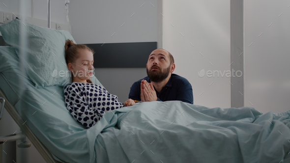 Sick girl daughter sleeping after surgery recovery while worried father praying for kid ...