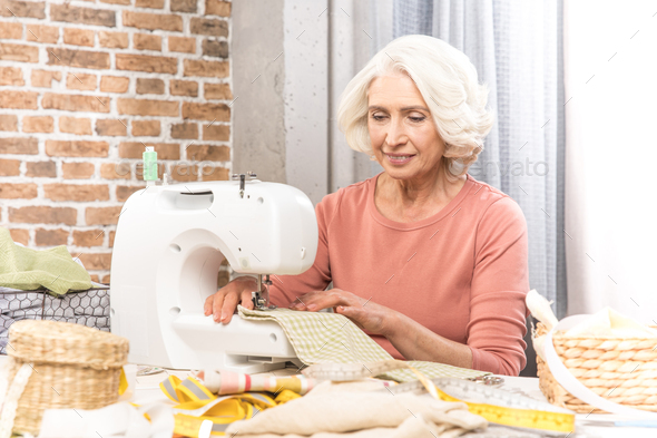 Senior woman sewing clothes with sewing machine and smiling Stock Photo ...