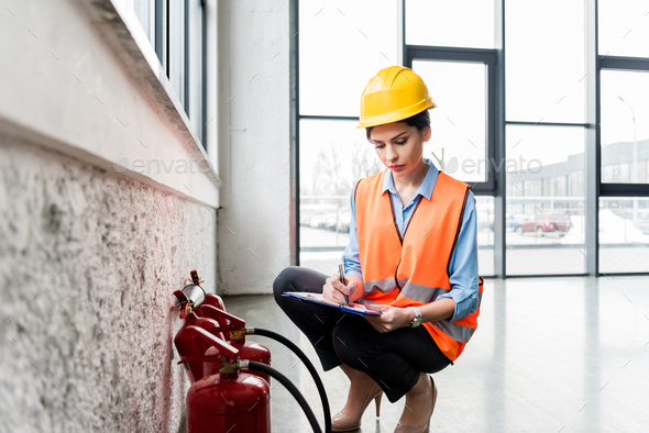 beautiful firefighter in helmet writing on clipboard while checking ...