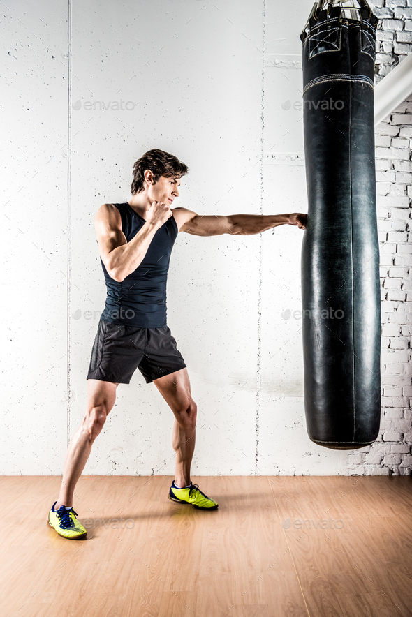 Full length portrait of muscular male kickboxer boxing in punching bag ...