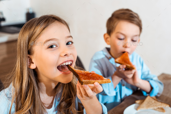 selective focus of cheerful siblings eating toast bread with bread ...