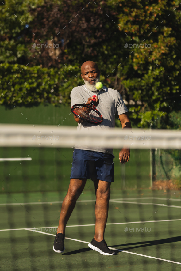 Senior african american man playing tennis striking ball on tennis ...
