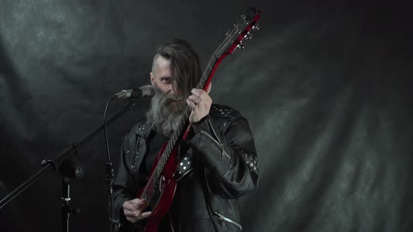 Bearded lrock musician in leather jacket plays red electric guitar and ...