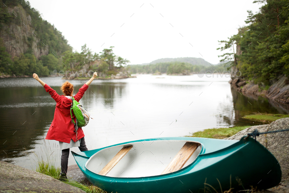 portrait from behind woman standing next to canoe with arms raised ...