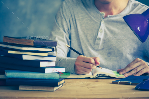 Close up of a man writing in notebook, Stack of old books on wooden ...