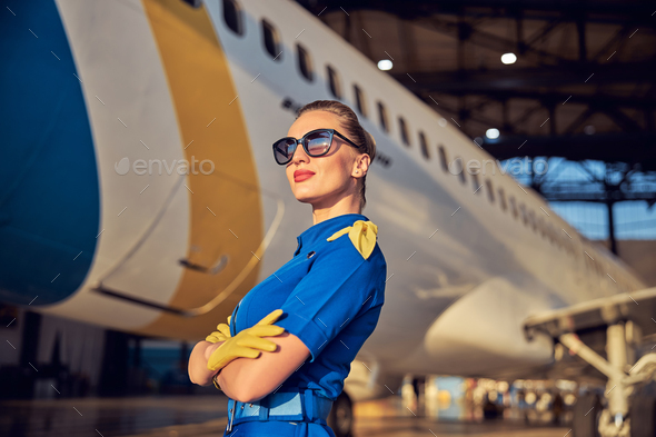 Elegant female air hostess crossing her arms in the hangar at the ...
