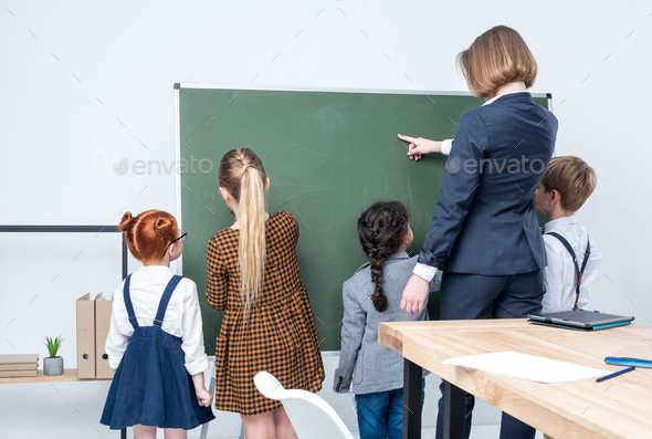 back view of young female teacher with multiethnic students standing at ...
