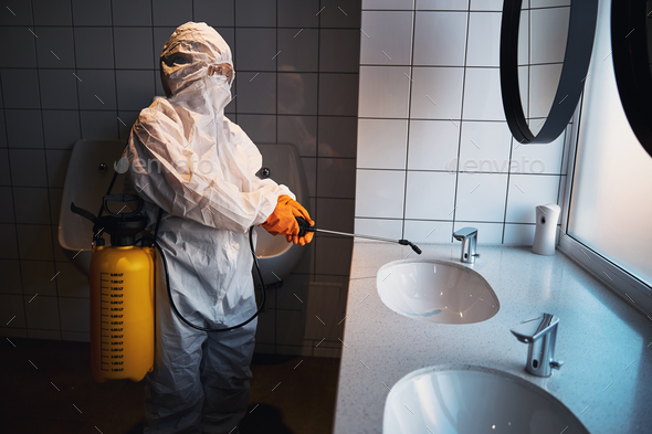 Professional female cleaner in a hazmat suit disinfecting surfaces ...