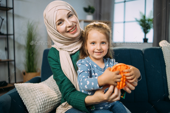 Cute girl child is sitting with her Arab mother on the sofa at home ...
