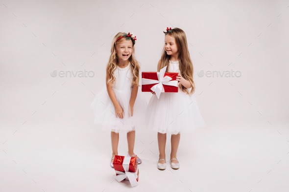 two little girls in white dresses with Christmas gifts on a white ...
