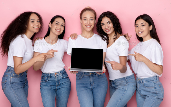 Diverse Women Holding Laptop Pointing At Empty Screen, Pink Background ...