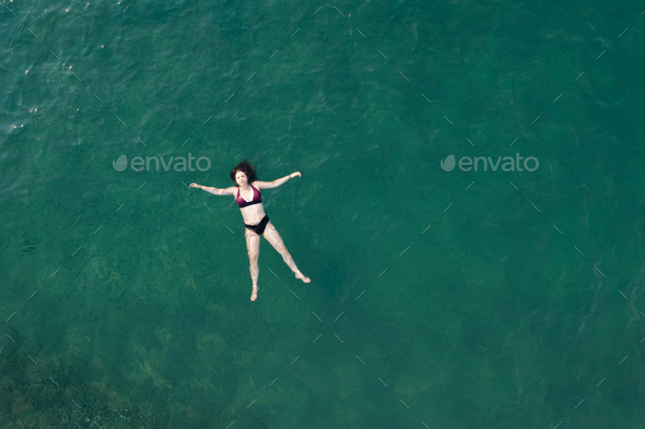 Woman with swimsuit floating and swimming in blue sea. Overhead shot ...