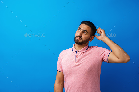 Pensive young arab man thinking and looking up against blue background ...