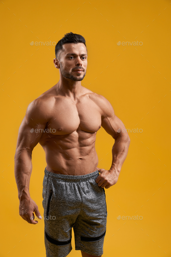 Strong bodybuilder keeping hand on waist Stock Photo by serhiibobyk