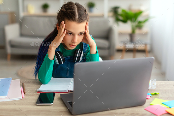 Tired school girl doing homework grabbing her head using laptop Stock ...