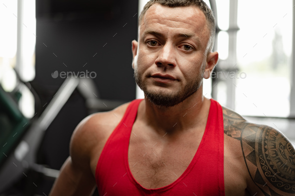 Portrait of man bodybuilder in red shirt in gym Stock Photo by FabrikaPhoto