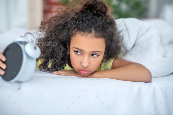 Awakened girl with brown eyes looking at the alarm clock. Stock Photo ...