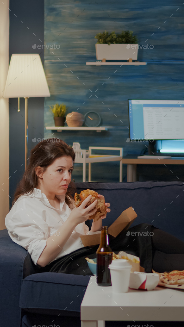 Young woman laying on couch eating burger and laughing Stock Photo by ...