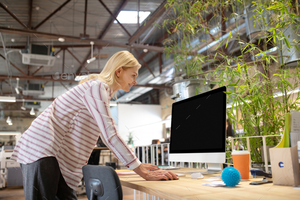 Blonde woman bending over desk, looking at screen. Stock Photo by ...