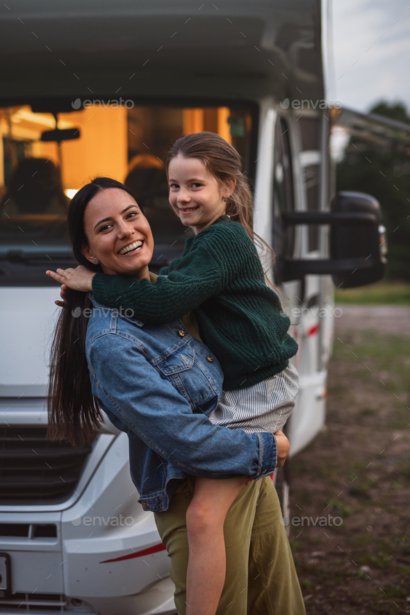 Mother with daughter standing by car outdoors in campsite at dusk ...