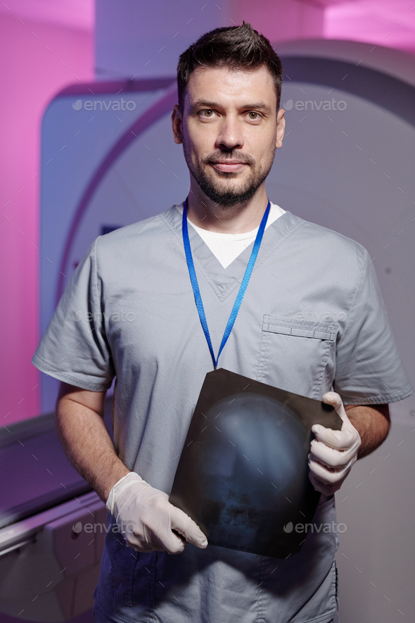 Confident radiologist in gloves and uniform standing against medical ...
