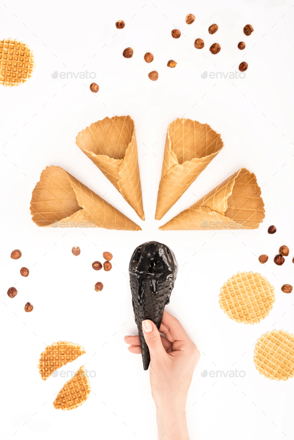 cropped image of woman holding black ice cream in cone under empty ice ...
