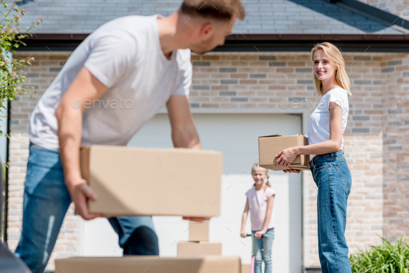 couple carrying cardboard boxes for relocation into new house and their ...