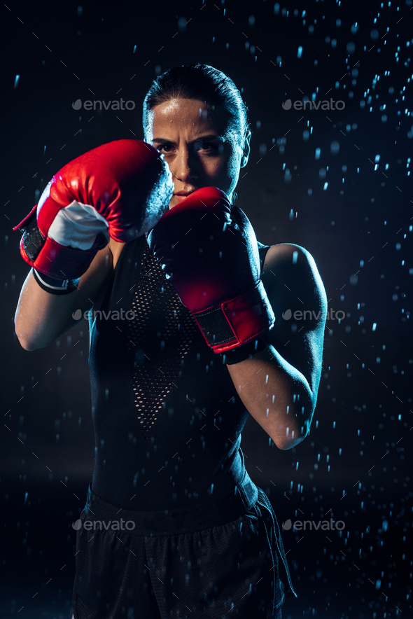 Concentrated boxer in red boxing gloves standing under water drops on ...