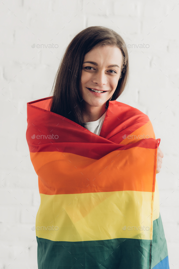 happy transgender woman covering with pride flag and looking at camera ...