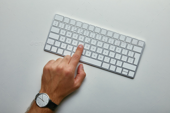 Cropped view of man pushing button on computer keyboard on grey ...