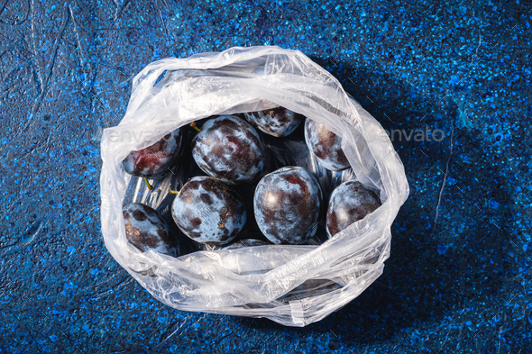 Fresh ripe plum fruits in plastic bag package on blue abstract ...