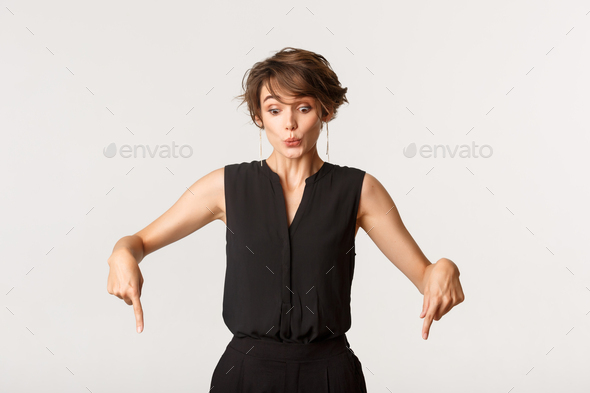 Curious attractive woman looking and pointing down with intrigued ...
