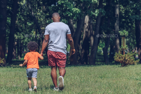 back view of african american father and son holding hands while ...