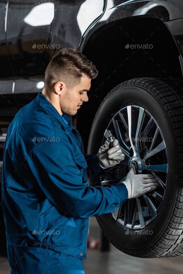 mechanic looking at screw nut while fixing wheel on car Stock Photo by ...