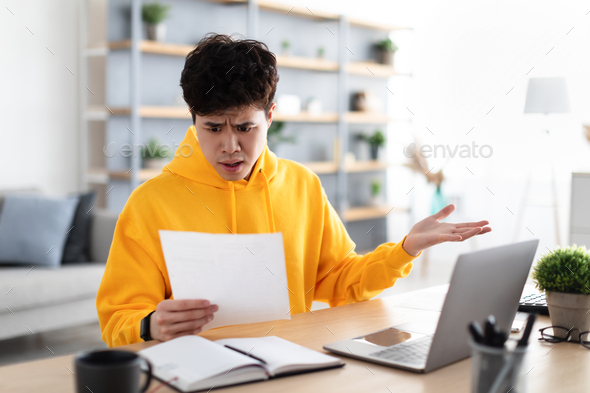 Confused asian man holding paper reading report working on laptop Stock ...