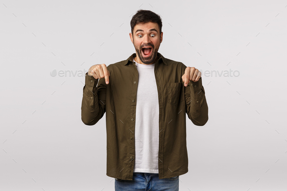Excited, happy and cheerful handsome bearded man in coat, pointing down ...