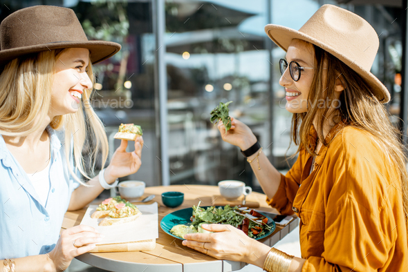 Girlfriends eating healthy food on a terrace Stock Photo by RossHelen