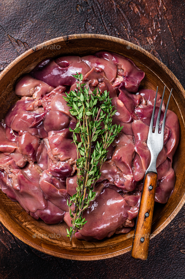 Raw chicken liver offals in a wooden plate. Dark background. Top view ...