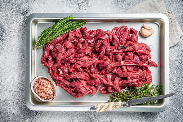 Raw Beef strips slices in a kitchen tray with rosemary and thyme. White ...