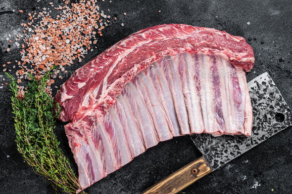Raw rack of lamb ribs on butcher cutting board with herbs. Black ...