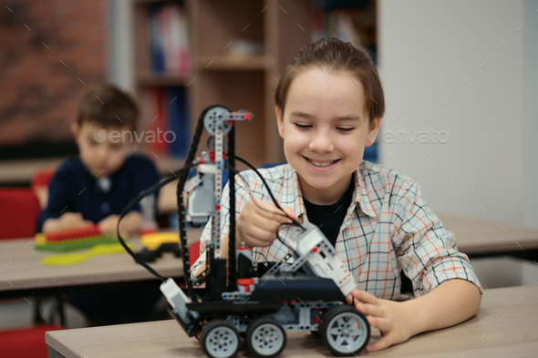 Two boys kids of different age playing with robot toy at school ...