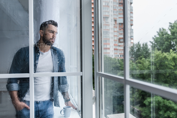 Depressed sad man looking through window, hoping for end of pandemic ...