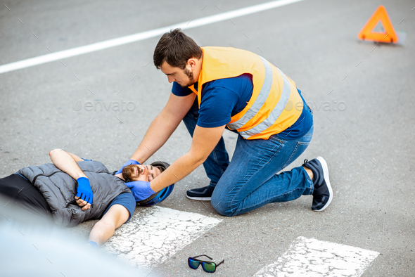 Road accident with injured cyclist and man providing first aid Stock ...