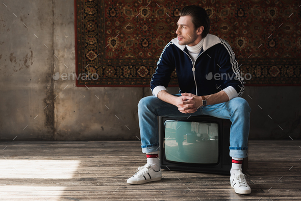 thoughtful young man in vintage clothes sitting on retro tv set in ...