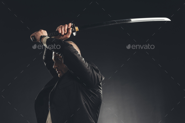 side view of man in suit making hit with katana sword isolated on black ...