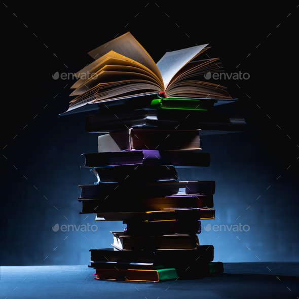 stack of colored books with open book on top on dark surface Stock ...